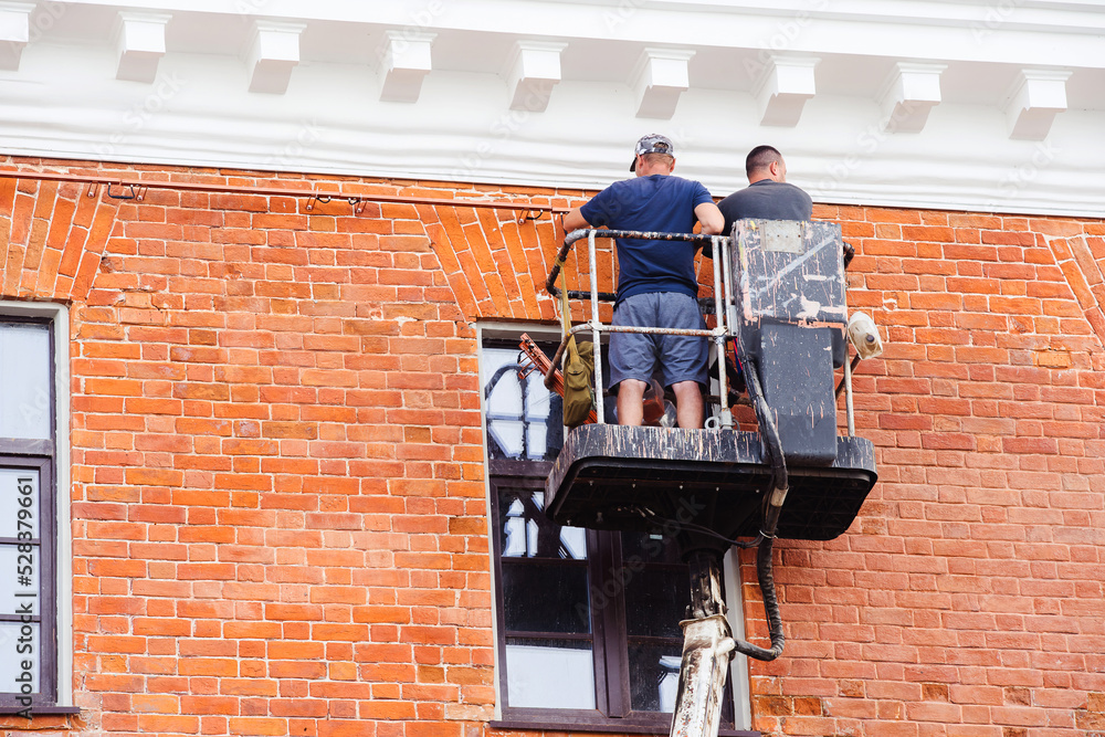 Repair of the facade of a brick house. Two workers on an aerial ...