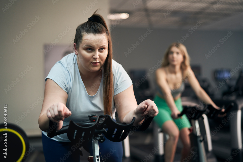 Overweight caucasian woman riding a bike at the gym Stock Photo | Adobe ...