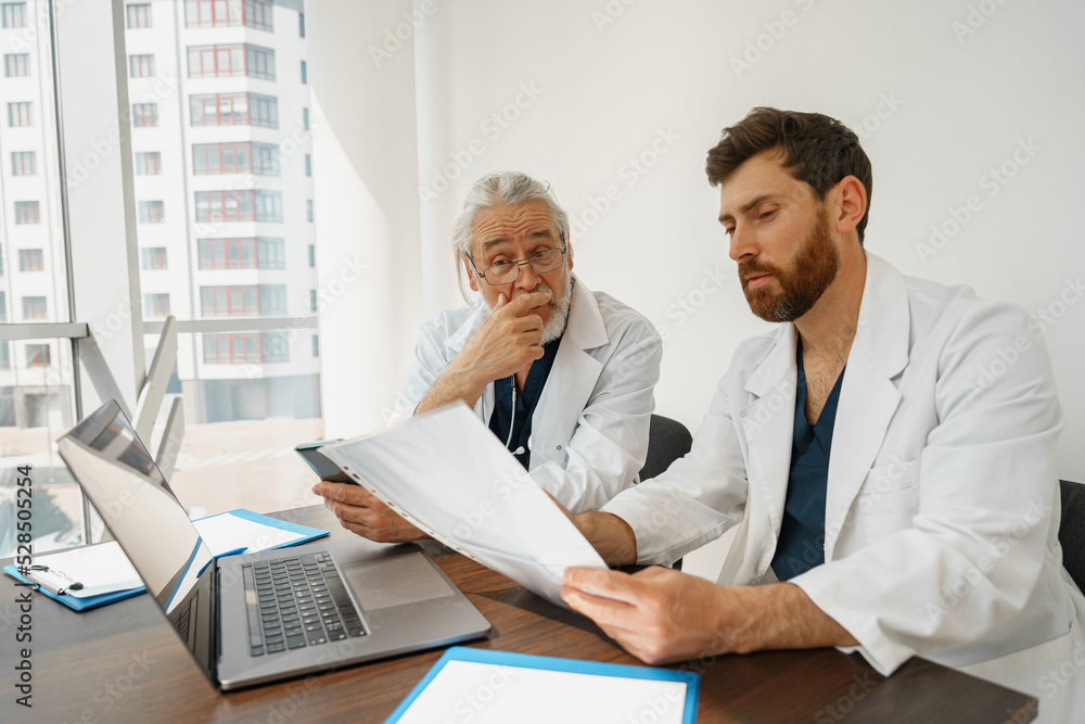 Two doctor colleagues discussing patient diagnosis sitting in office of ...