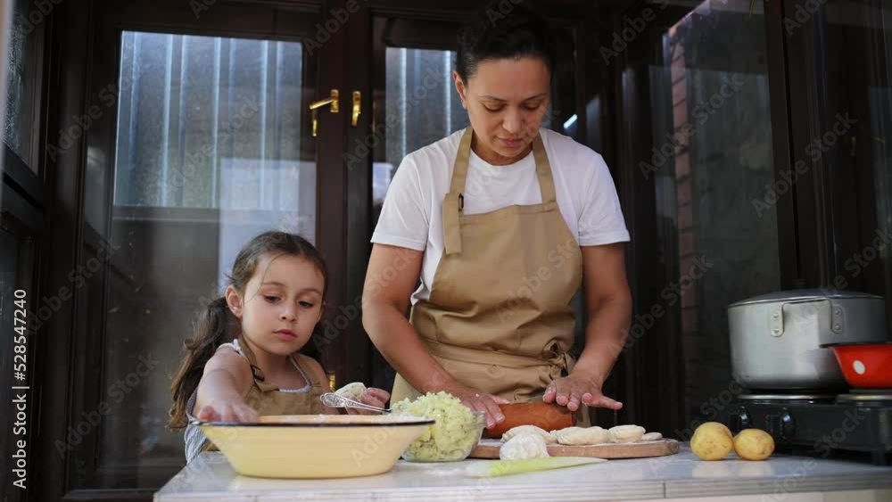Pretty mom and daughter wearing beige chef's apron, cooking dumplings ...