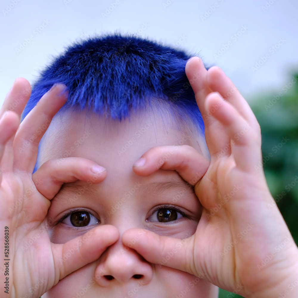 child on natural green background, boy 8-9 years with blue hair smiles ...