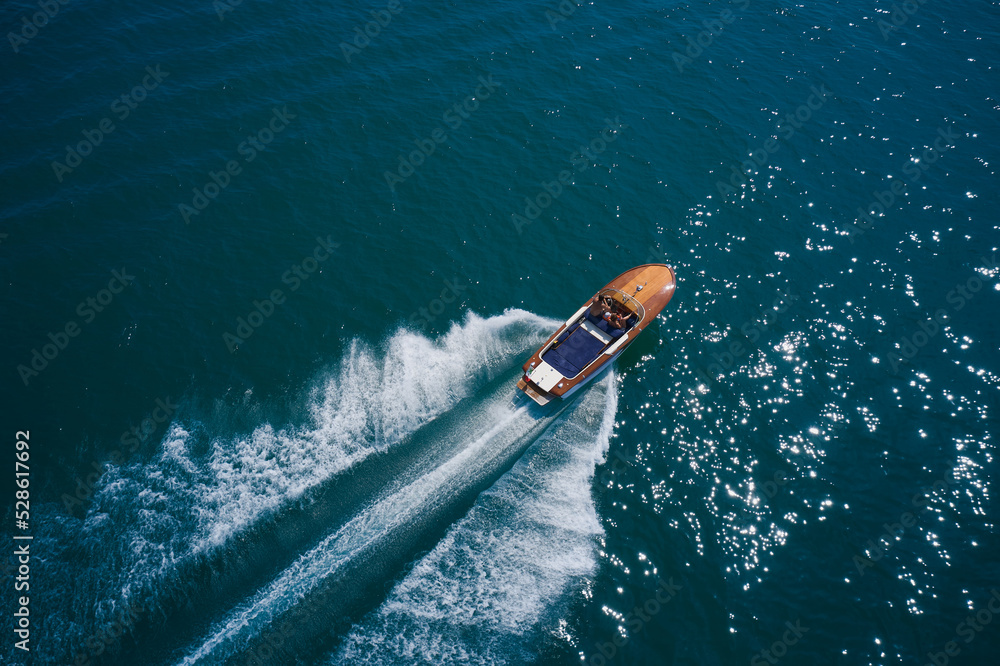 Classic wooden boat with motor moving on blue water aerial view ...