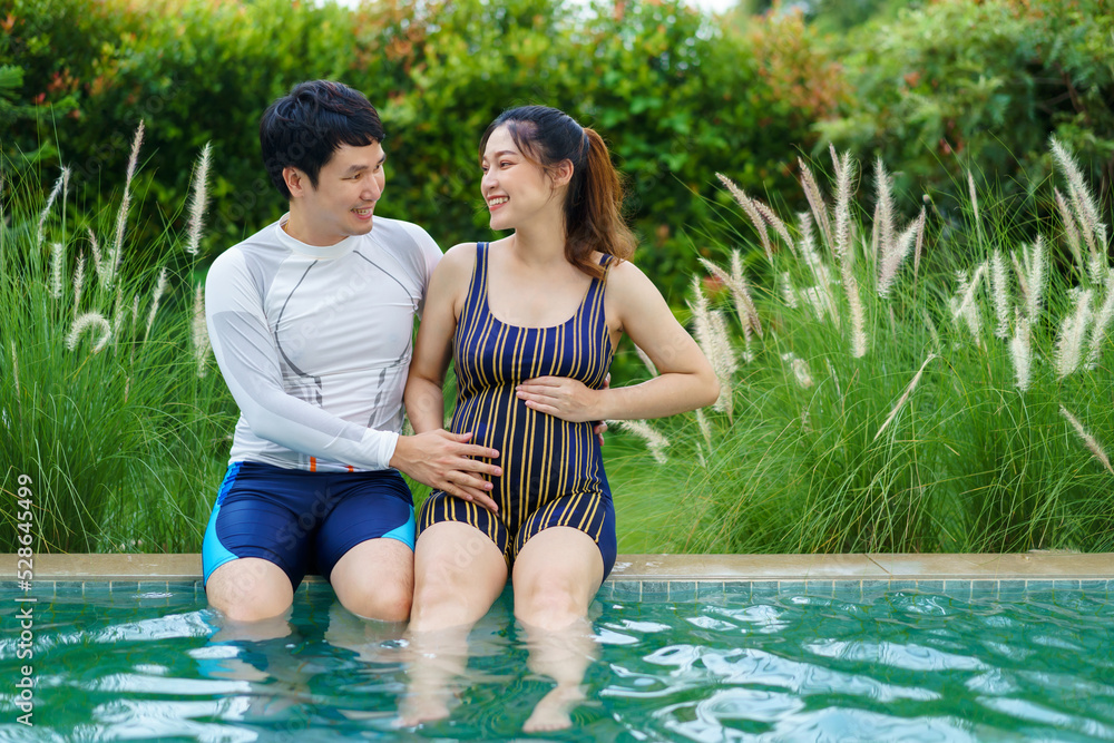 happy pregnant woman and her husband in swimsuit sitting on edge of ...
