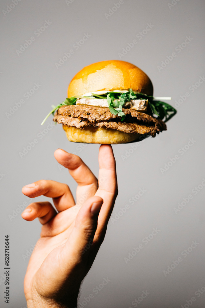 Human hand holding with a finger a doble burger with old dry cheese and ...