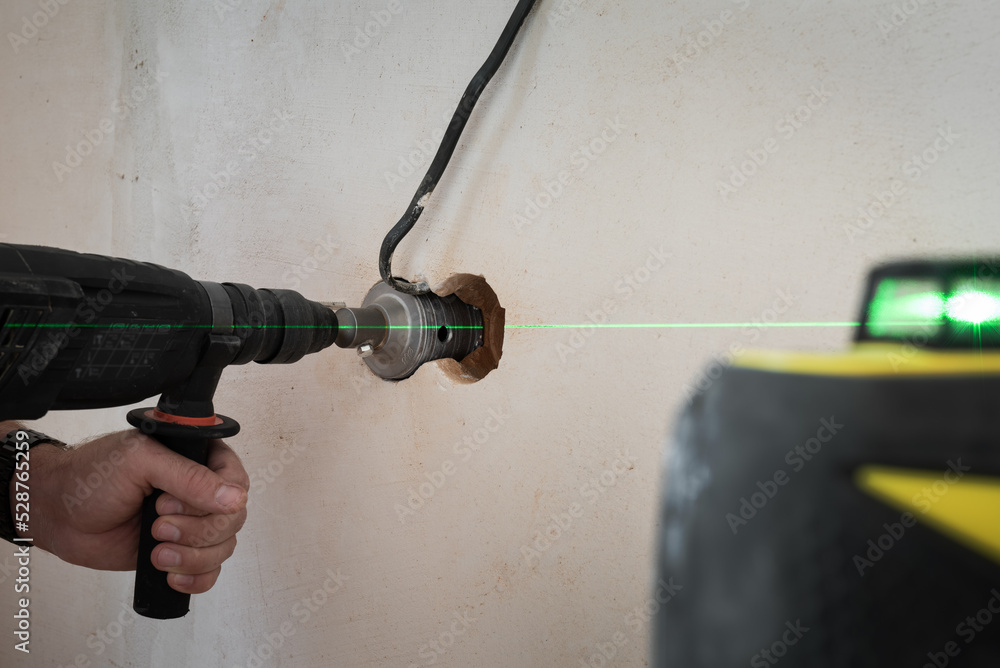 Electrical wiring work using laser level device. Man drilling round ...