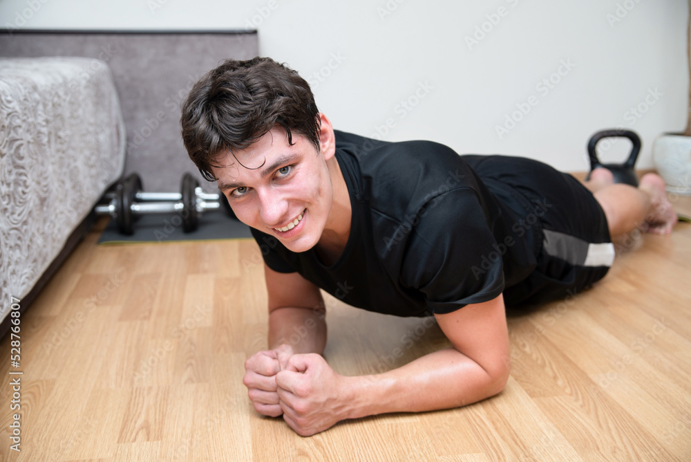A young teen guy, does sports at home, stands in static plank position ...