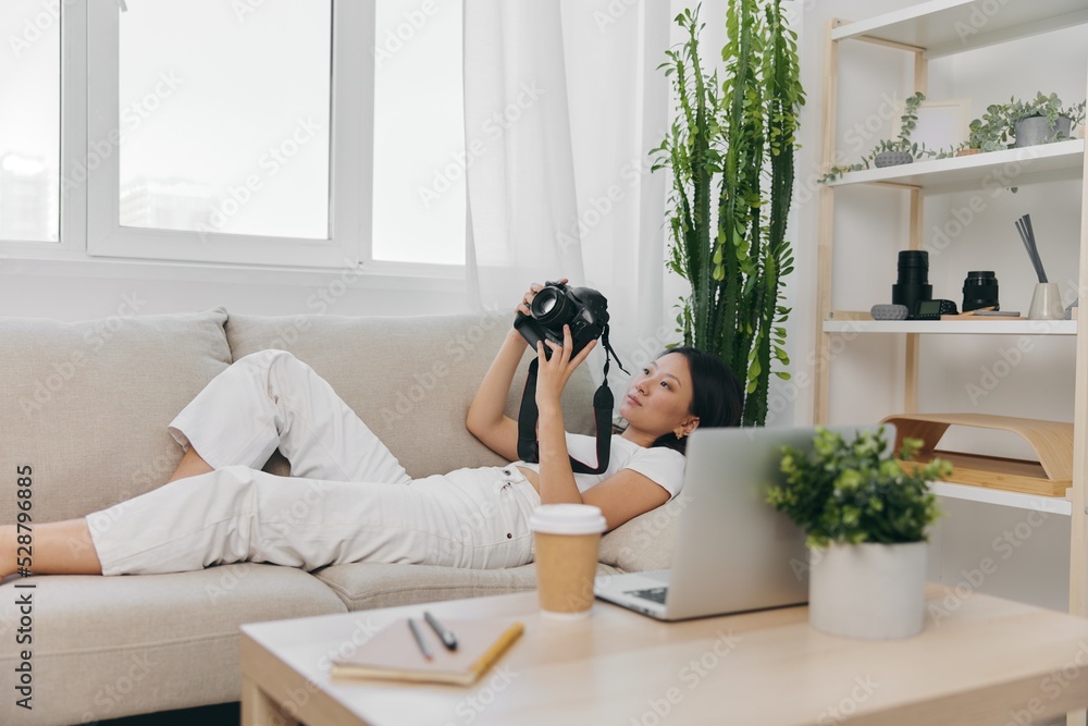 An Asian woman photographer lies on the couch with a camera and watches ...
