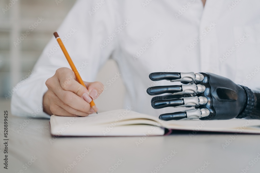 Disabled female writing with pencil in notebook, using bionic ...