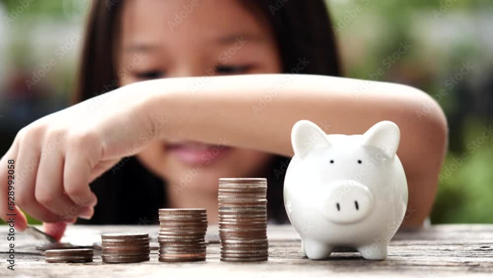 Saving Money Concept. Happy Asian child girl save money by putting ...