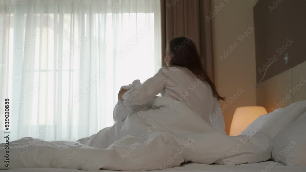 Woman wakes up in early morning stretching arms in hotel room. Female ...