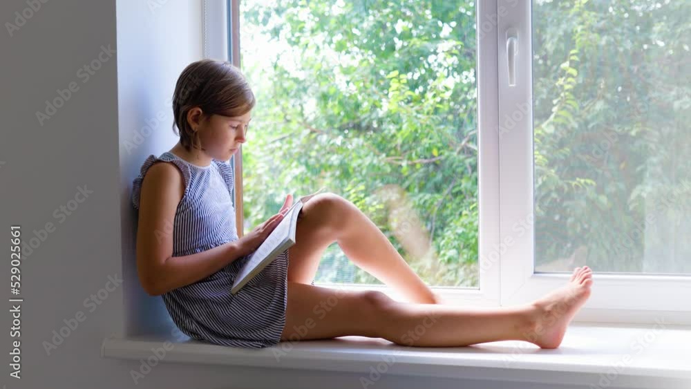 Side view of pretty child serious read book sitting on windowsill ...
