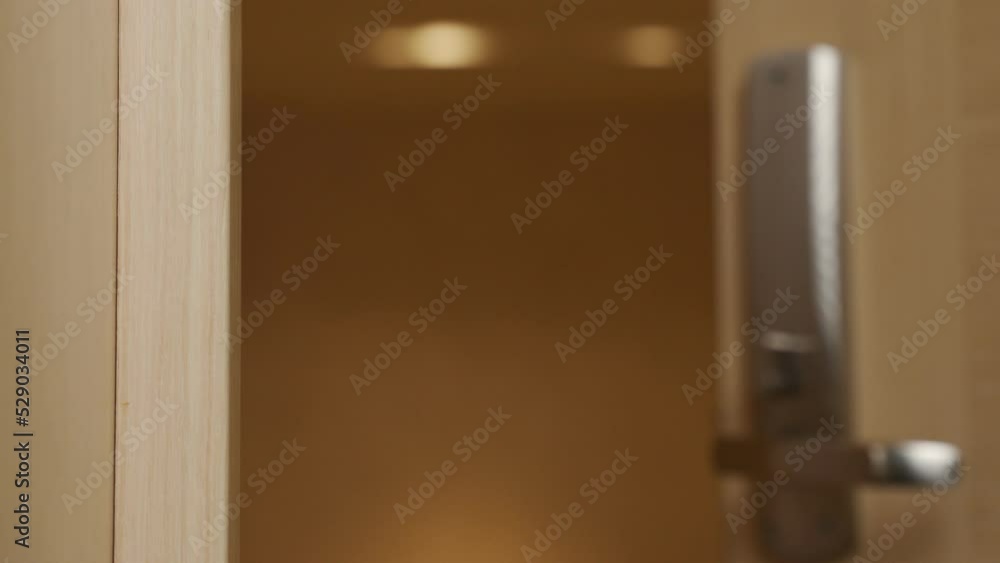 Woman turns safety knob on metal lock to open wooden door to corridor ...