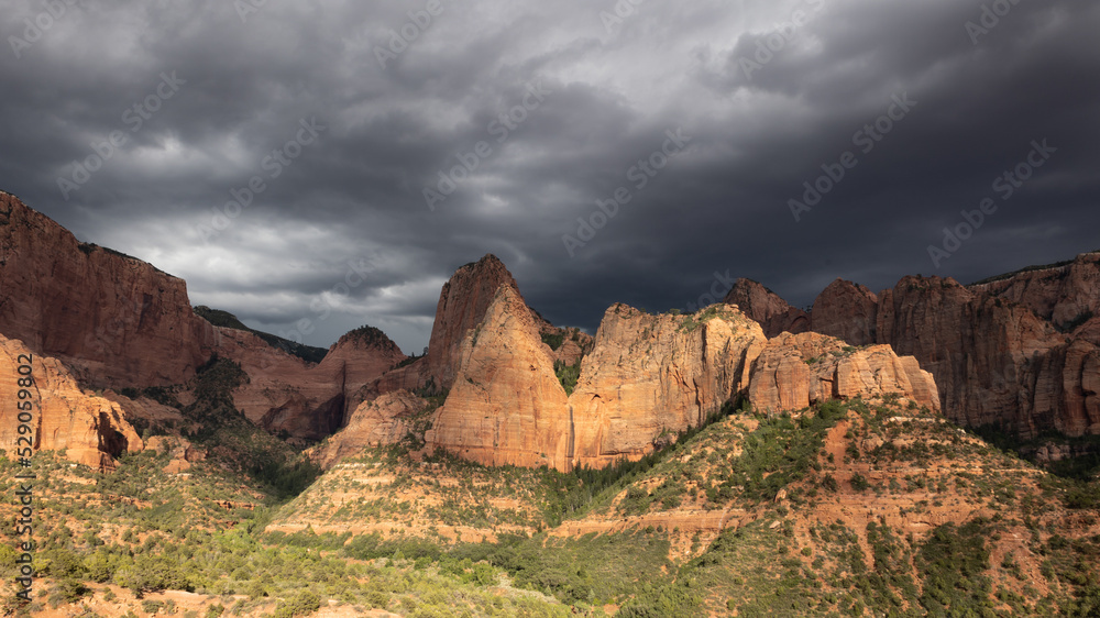 Dark storm clouds cast deep shadows over the mountains in Kolob canyon ...