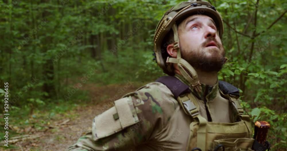 an armed soldier in body armor and a helmet falls to his knees and ...