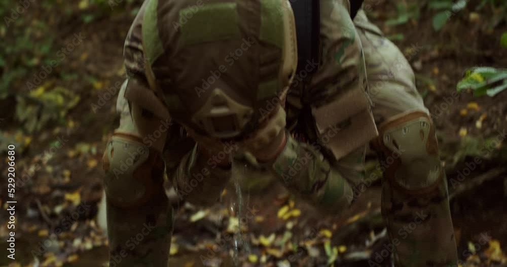 an armed soldier washes his face in the river. Ukrainian soldier in a ...