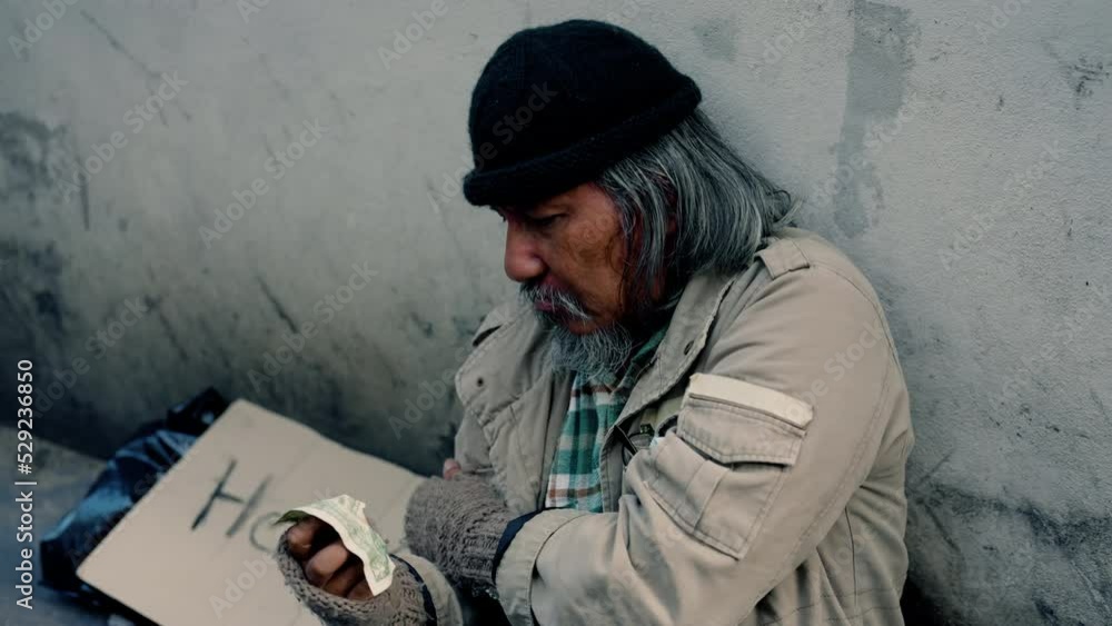 Video Stock 4k, An elderly Asian homeless man leaning against a wall ...