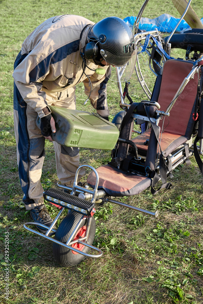 Professional paraglider in a helmet refuels the paraglider engine with ...