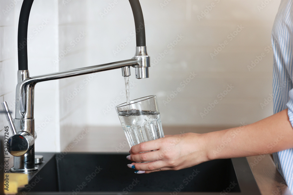 Woman filling drinking glass with tap water on the kitchen. Concept of ...