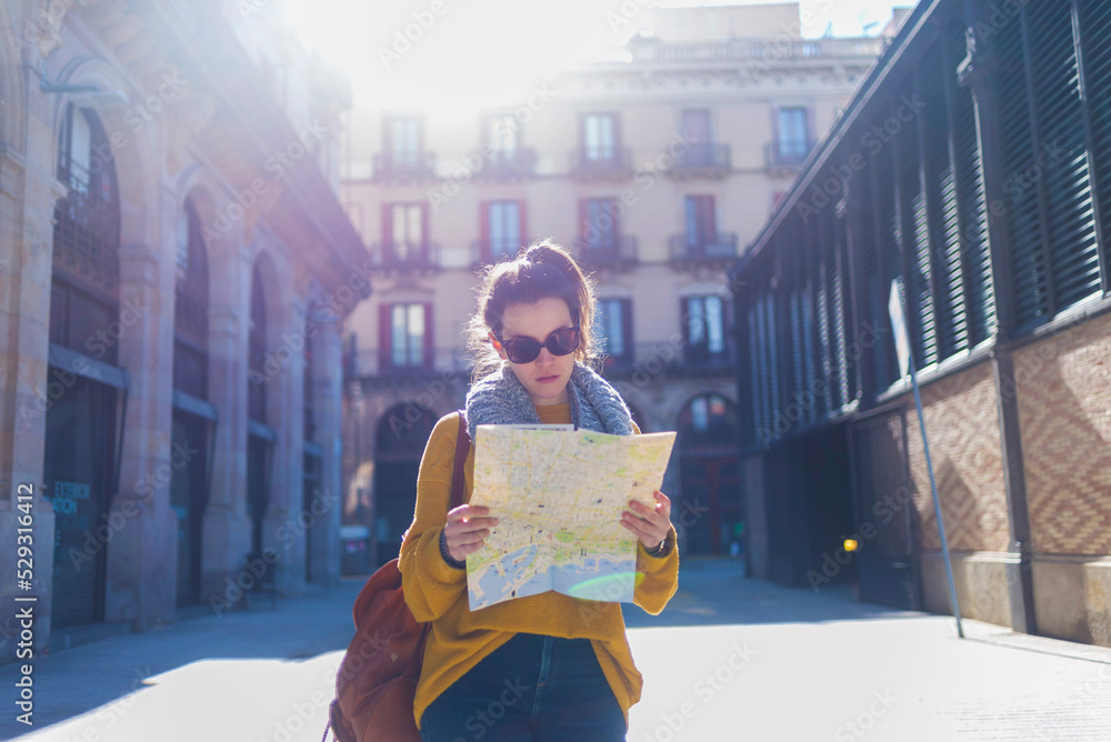 Female tourist reading map while standing against buildings in city ...