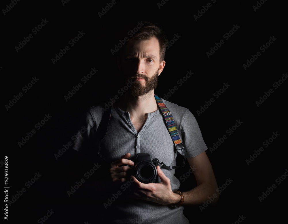 Portrait of confident man holding camera while standing against black ...