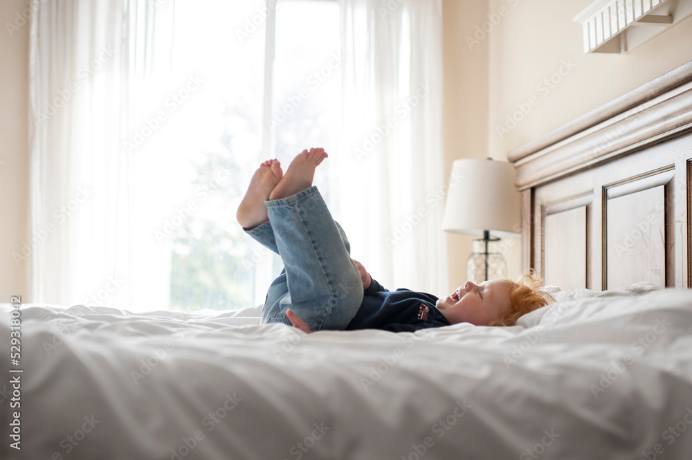 Baby boy giggling on bed in bedroom with feet up in the air Stock Photo ...