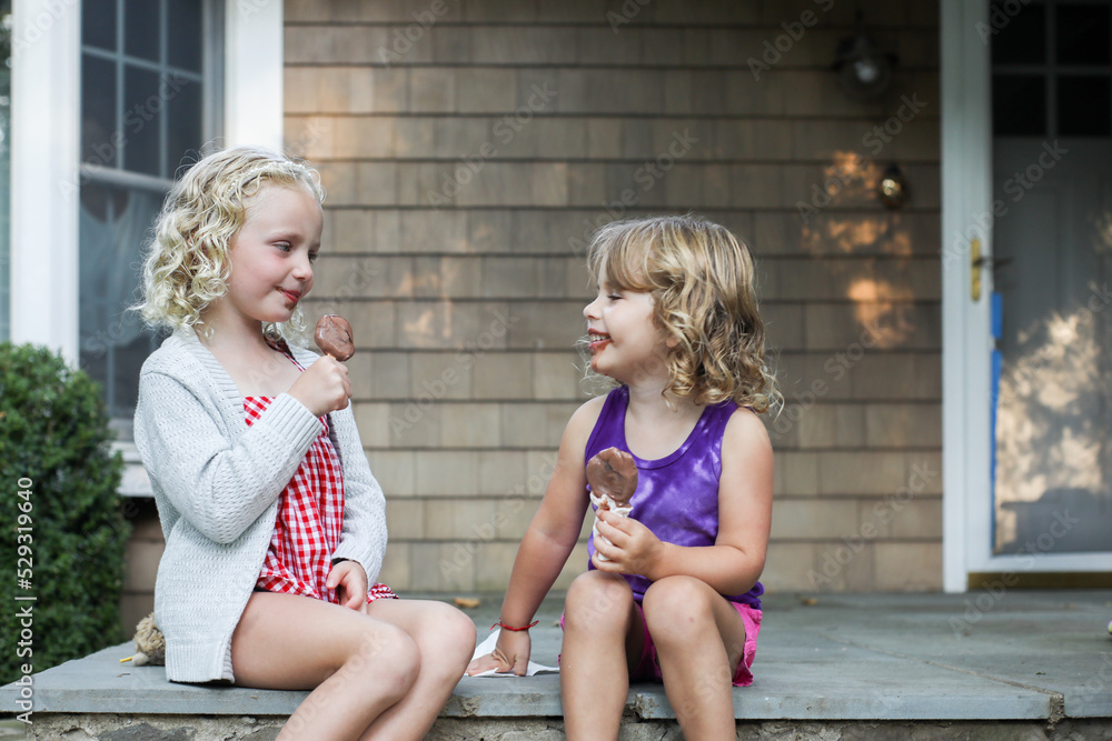 two girls sitting on porch steps eating ice pops in summer laughing ...