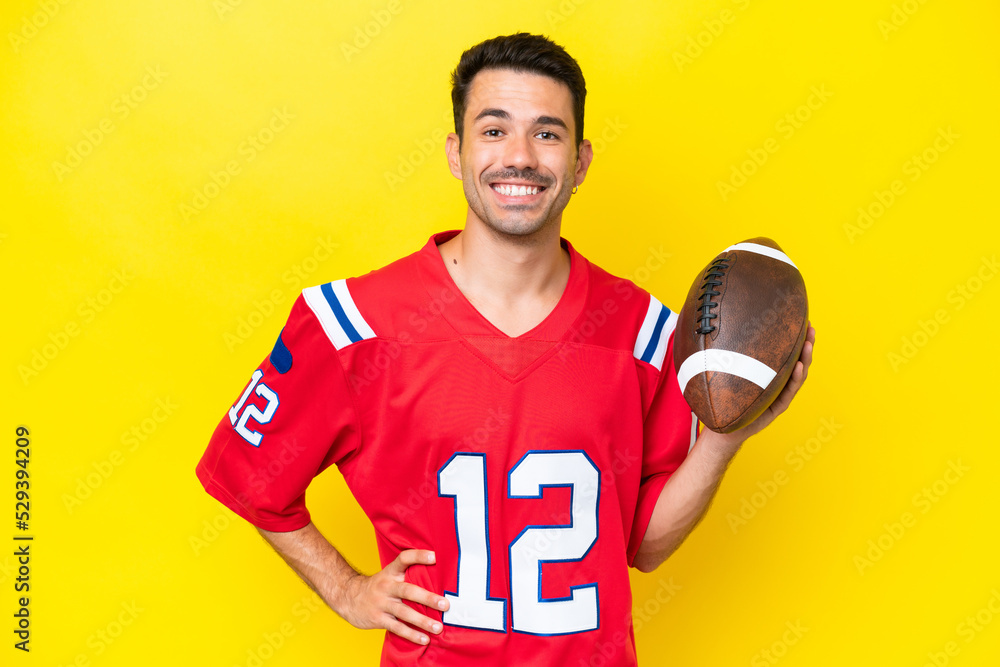 Young handsome man playing rugby over isolated yellow background posing ...