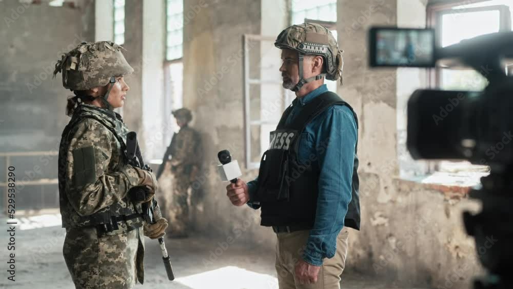 Male war journalist in bulletproof vest and helmet reporting live in ...