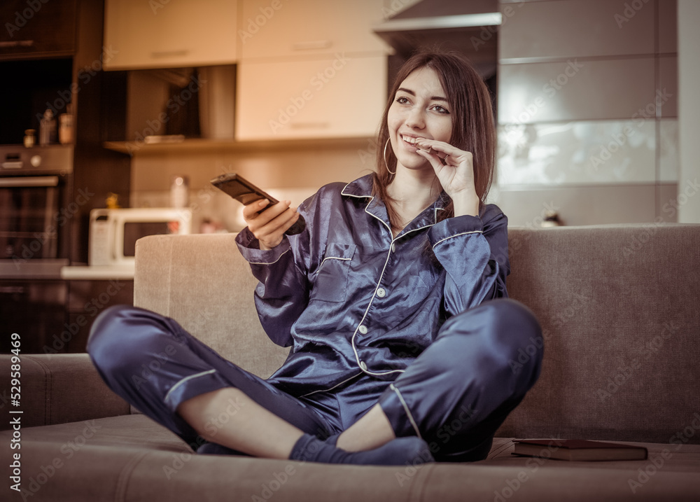 Young cheerful woman in a nightie switches TV channels with the remote ...
