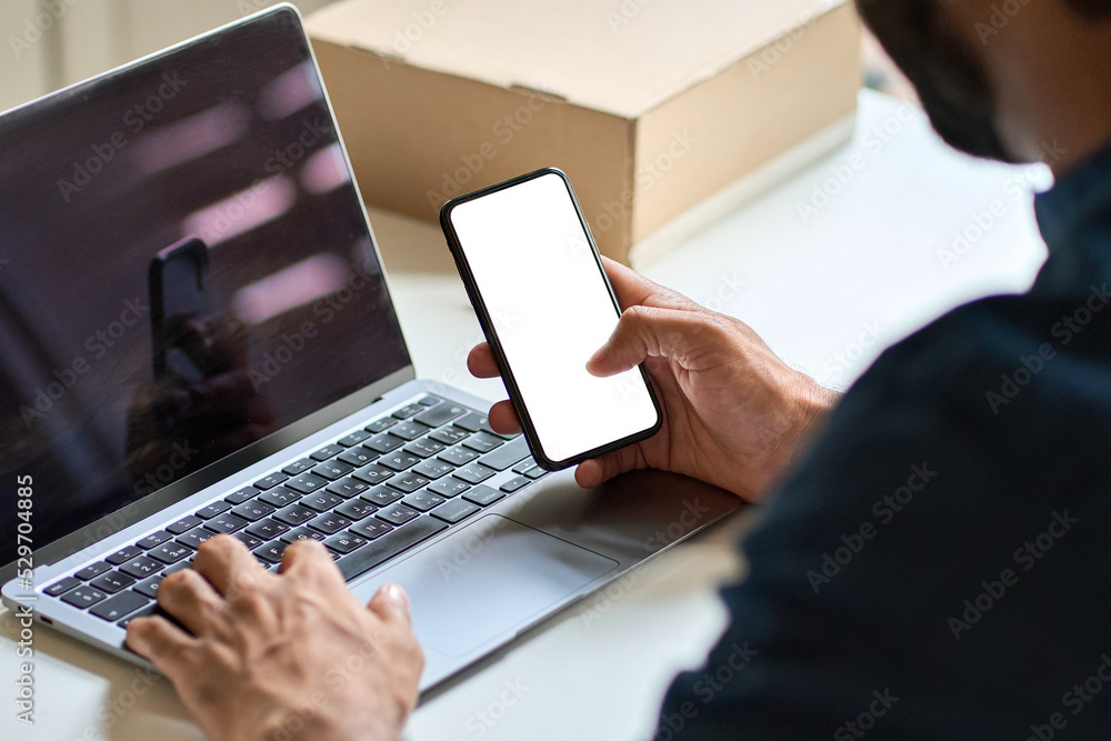 Male hand holding smartphone with white mock up screen using laptop at ...