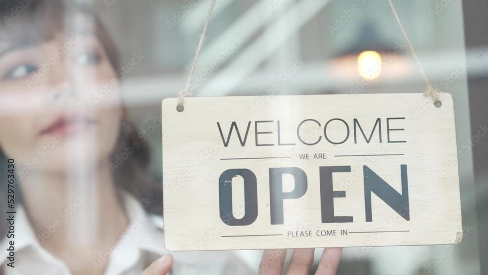 Close up female barista turning a sign from closed to open welcome sign ...