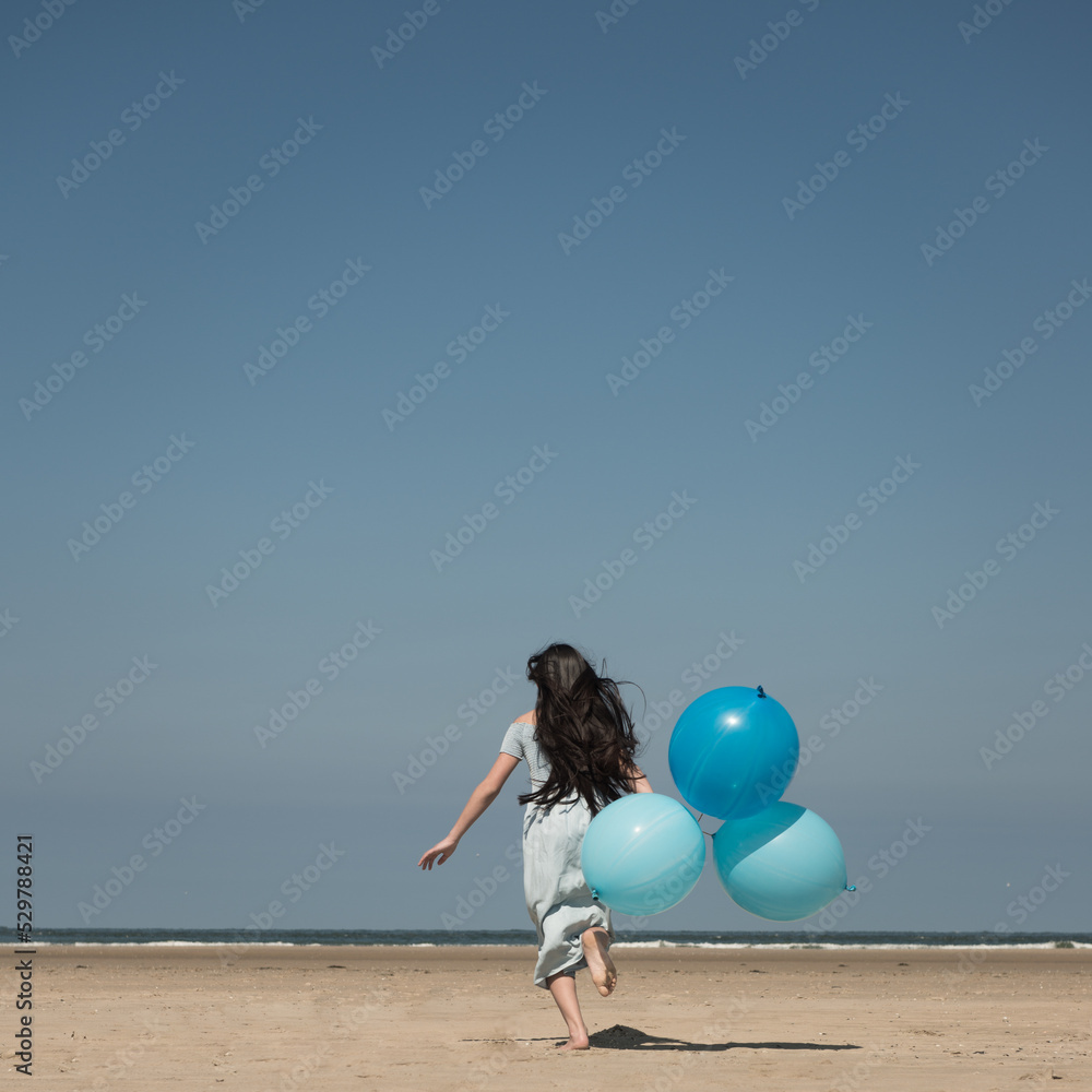 fine art portrait of girl in blue dress running with balloons on beach ...