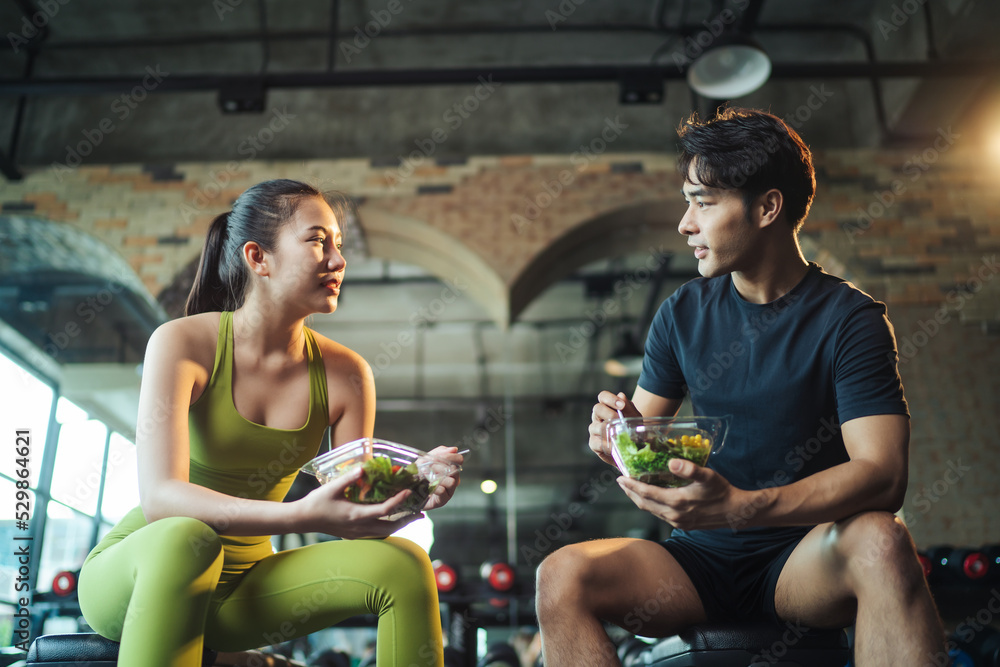 Two Asian people healthy eating salad after exercise at fitness gym ...
