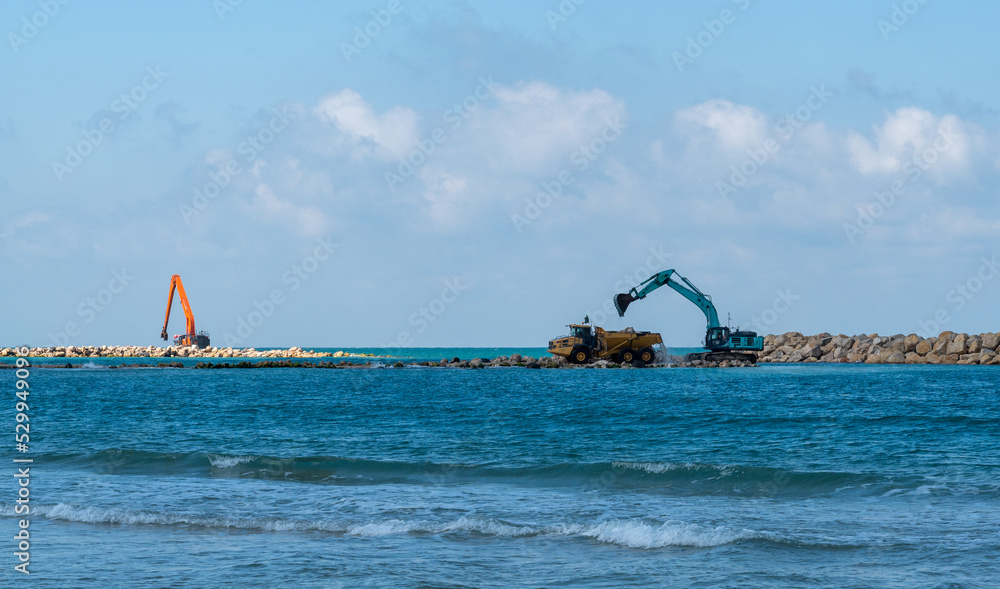 An excavator and a mining truck move stones into the sea. Construction ...