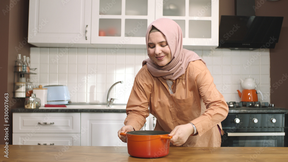 A young woman in a turban puts the pot on the dining table on the stove ...