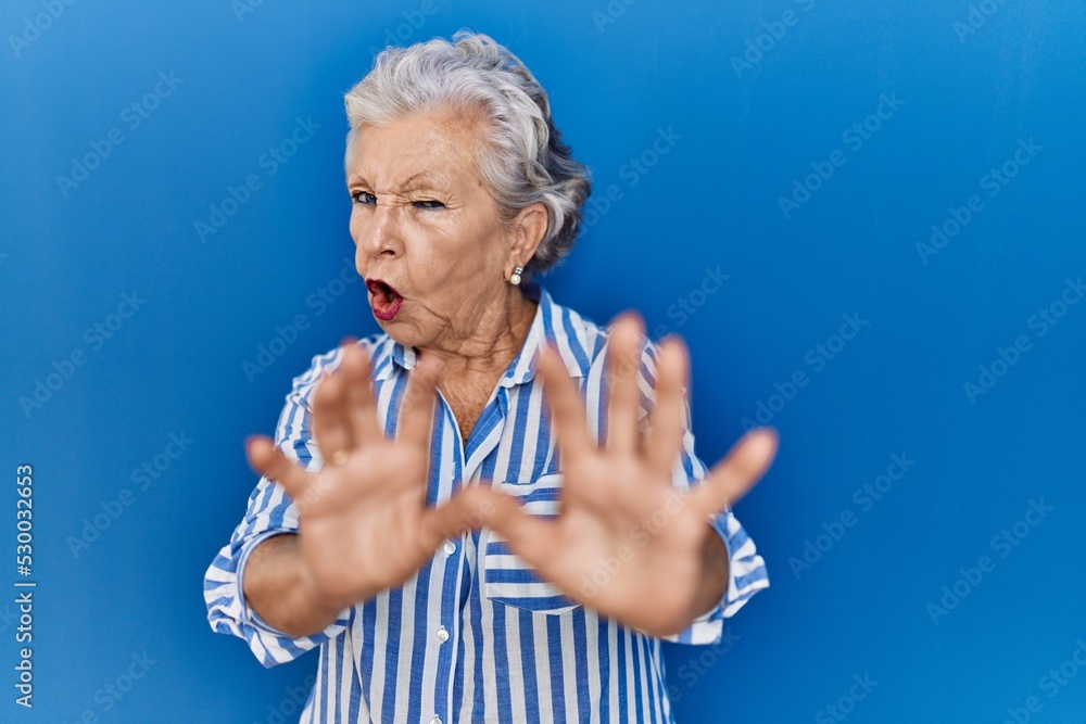 Senior woman with grey hair standing over blue background afraid and ...
