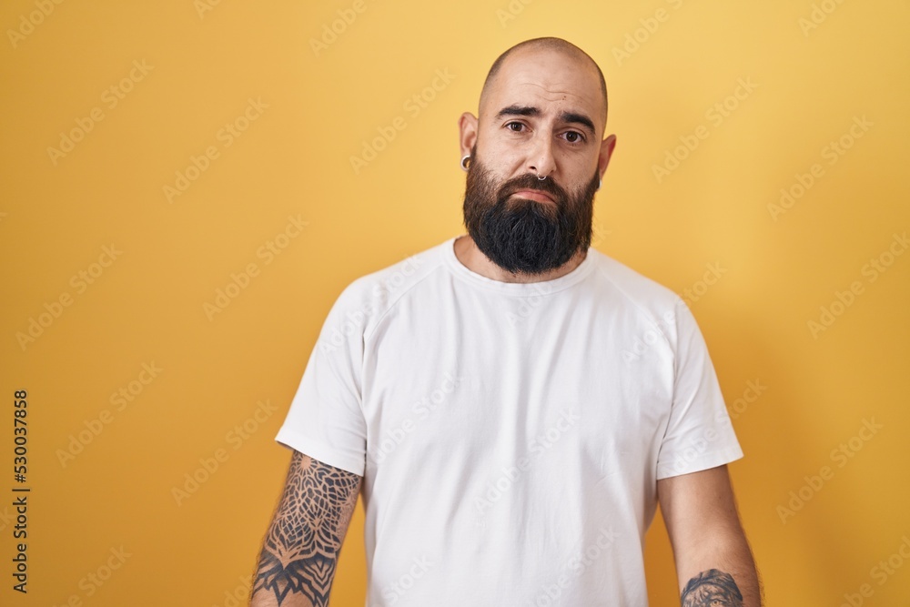Young hispanic man with beard and tattoos standing over yellow ...