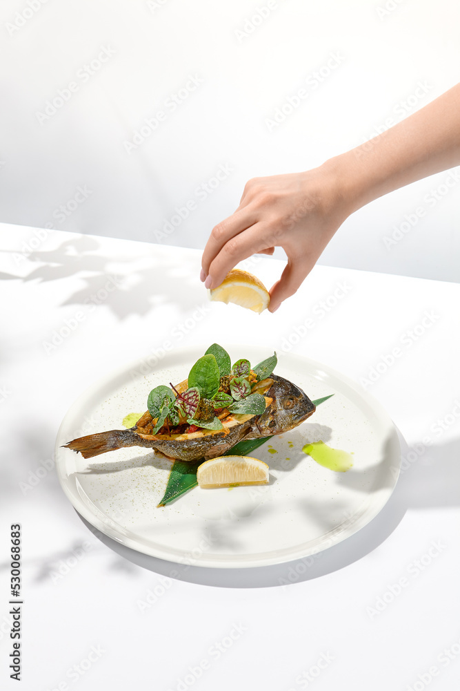 Roasted fish with female hand squeeze lemon. Person eat whole roasted ...
