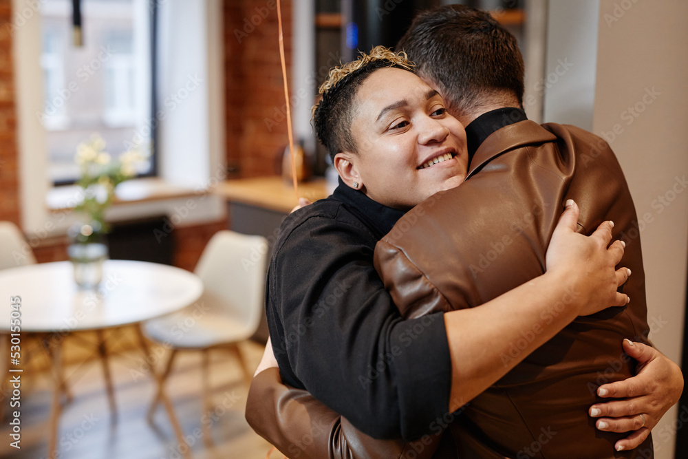 Happy young black woman in denim jacket giving hug to male friend while ...