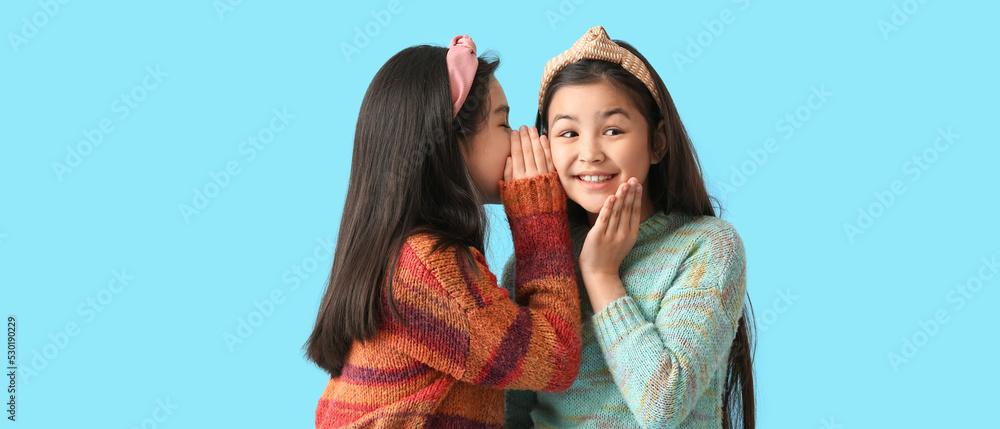 Cute little girl telling secrets to her sister on light blue background ...