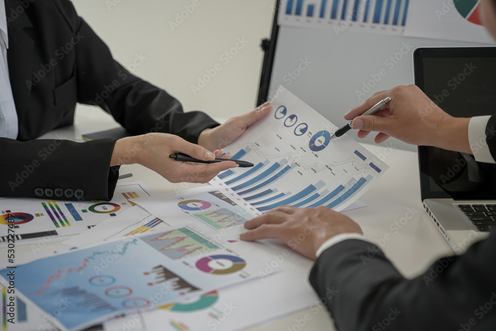 Business people gather for a brainstorming meeting pointing to a graph ...