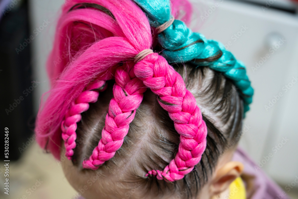The process of braiding fashionable braids from bright pink and blue ...