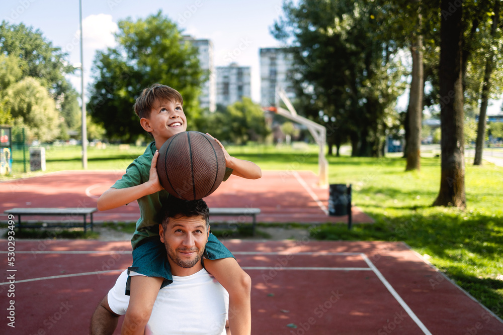 The father holds his son on his shoulders, helps him throw the ball ...