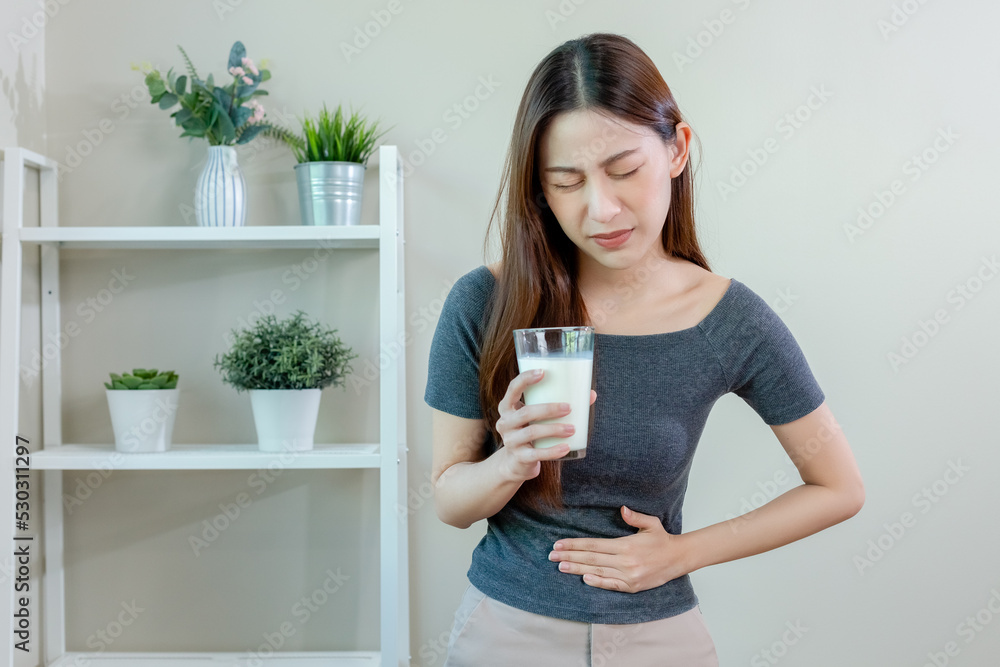 Asian female holding glass milk and hand touching abdominal area ...