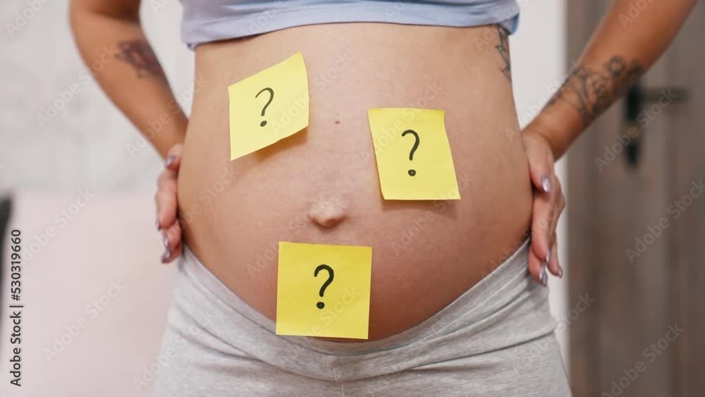 Question mark sticky notes on white pregnant woman's belly. Hands on ...