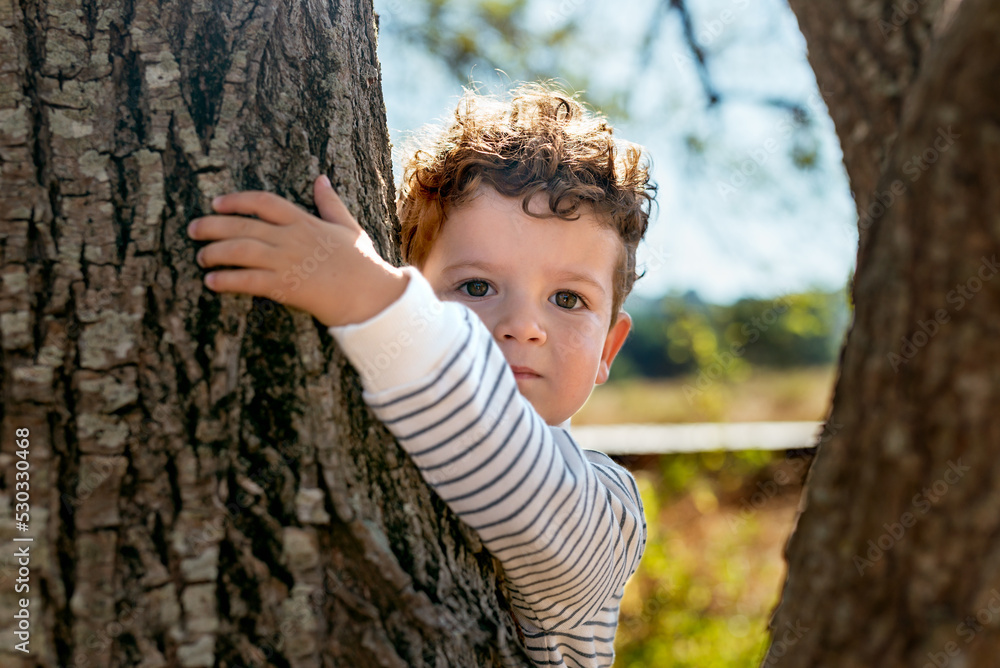 Little boy standing behind tree in nature Stock Photo | Adobe Stock