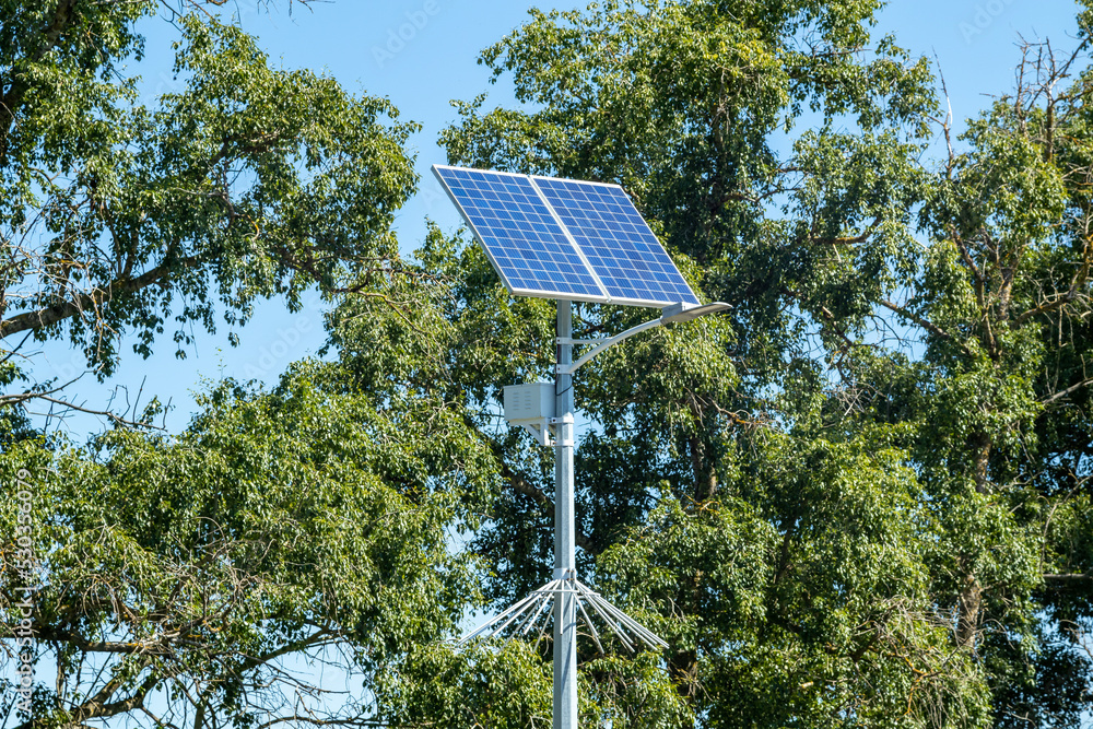 Lamp post with solar panel system on road with blue sky and trees ...