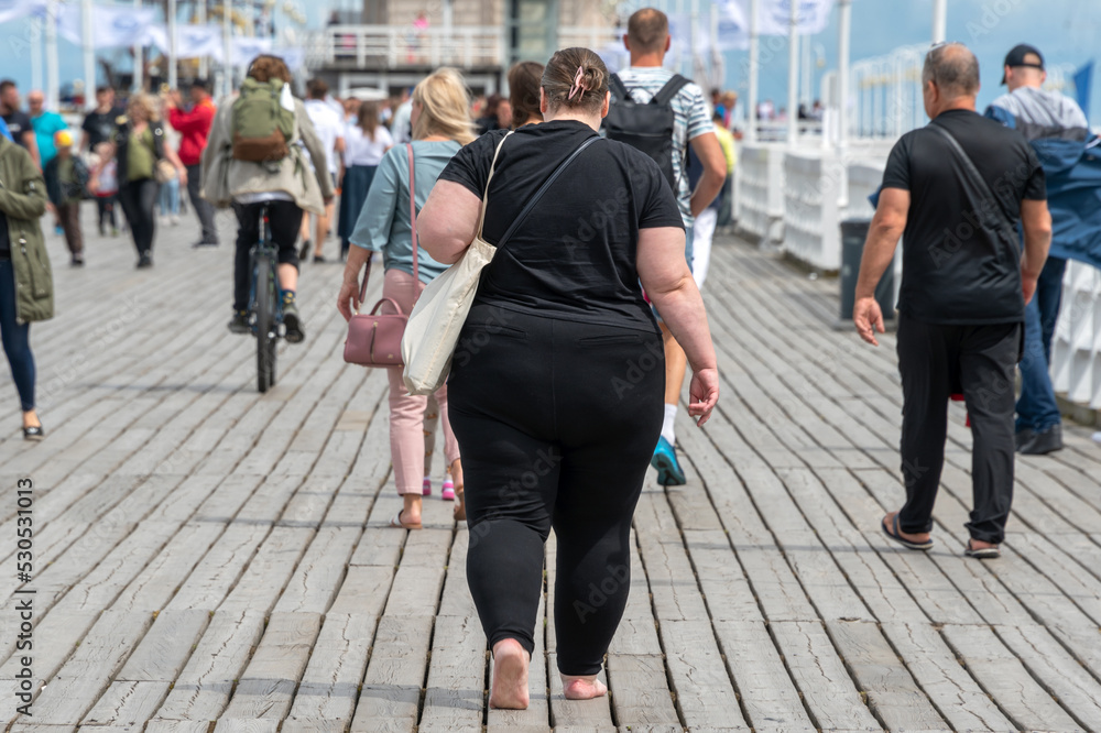 Overweight woman walking on the pier among people with normal weight ...