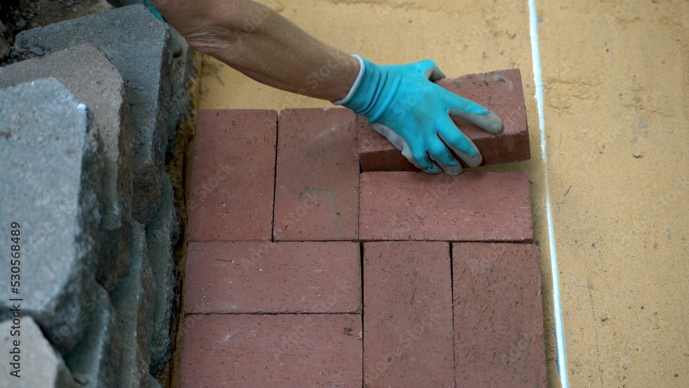 Overhead closeup of womans hand putting brick pavers onto a sand base ...