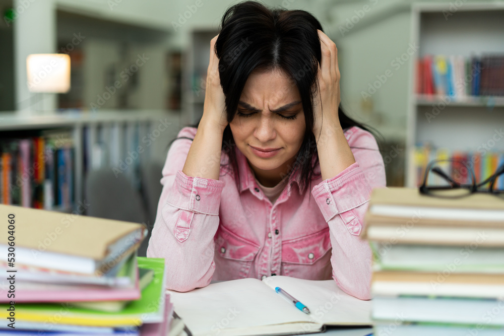 Anxious young woman with hands at her head feeling tired while studying ...